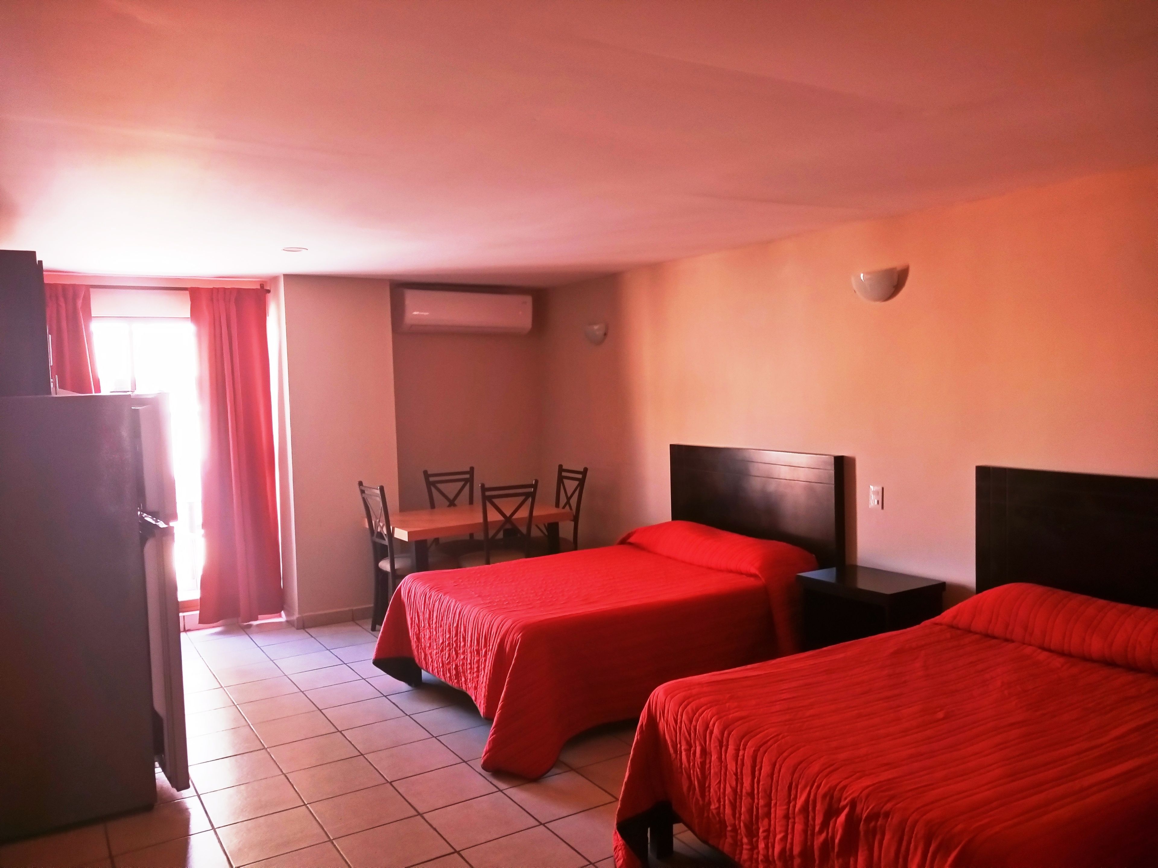 Quarto de hotel com duas camas, uma mesa de jantar com cadeiras, ar condicionado e um refrigerador.