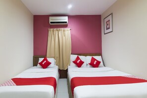 Quarto de hotel com duas camas, cortinas bege, almofadas vermelhas e um ar condicionado na parede.