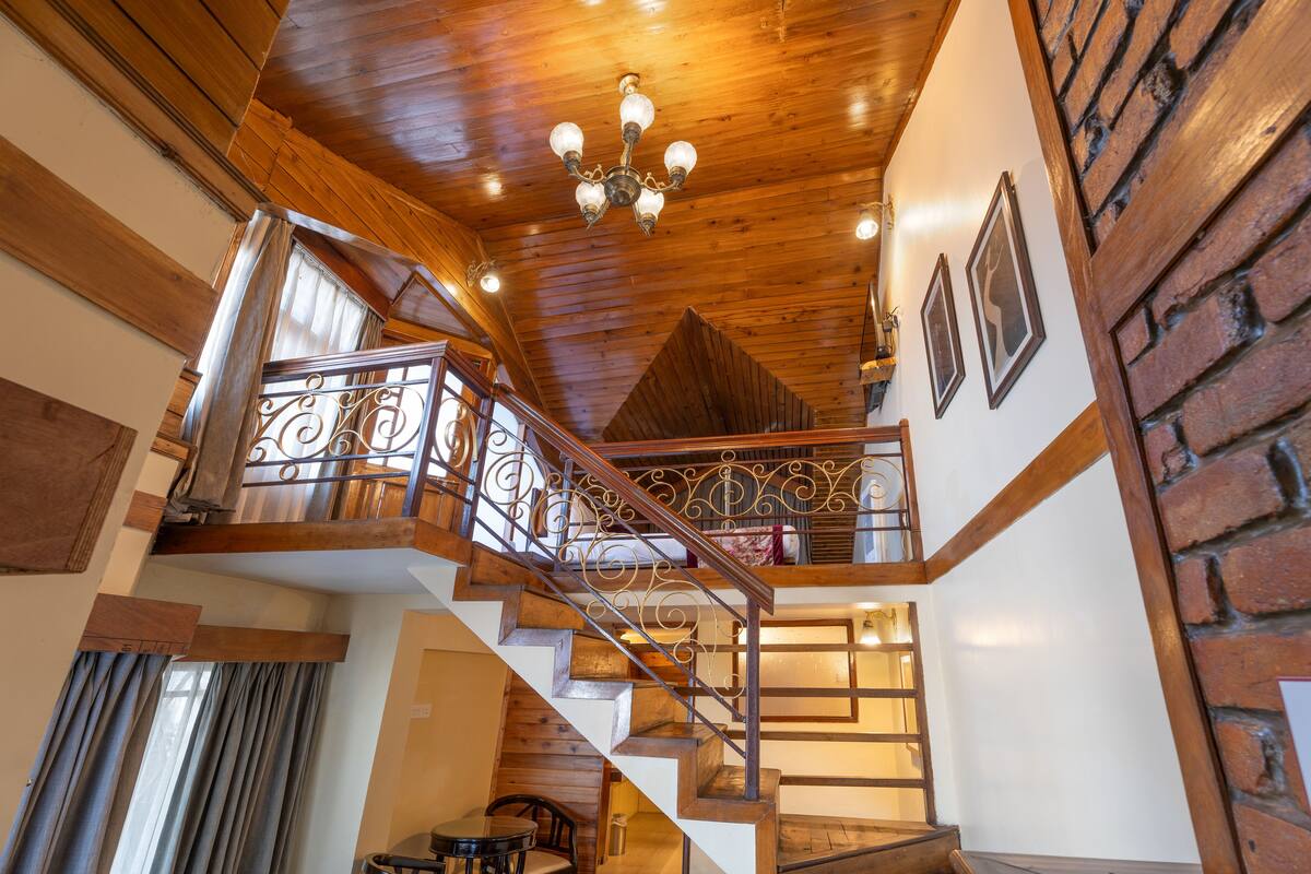 Interior em madeira com escadaria, candelabro e quadros nas paredes.