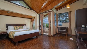 Quarto com teto de madeira, cama com roupa de cama floral, uma cadeira e uma escrivaninha com uma xícara.
