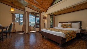 Um quarto espaçoso com uma cama grande, piso de madeira, uma escrivaninha e vista através de uma porta.