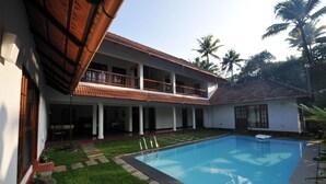 Um edifício de dois andares com piscina, alpendre coberto e área de jardim.