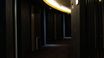 Um corredor pouco iluminado com teto curvo, piso coberto de carpete e uma lixeira.