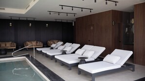 Uma área de piscina interna moderna com espreguiçadeiras, uma piscina e um teto com iluminação embutida.