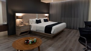 Quarto de hotel moderno com uma cama grande, mesas de cabeceira, uma escrivaninha e uma mesa redonda com um tabuleiro de objetos.