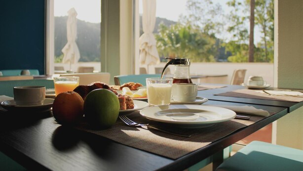 Uma mesa de café da manhã com frutas, uma cafeteira e vista para árvores e montanhas.