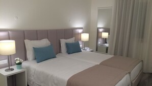 Quarto de hotel com duas camas, uma mesinha de cabeceira com abajur e um espelho.