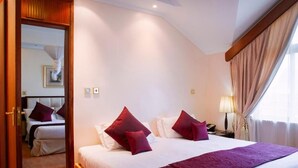 Quarto de hotel com uma cama grande, duas almofadas, mesa de cabeceira com abajur e janela com cortinas.
