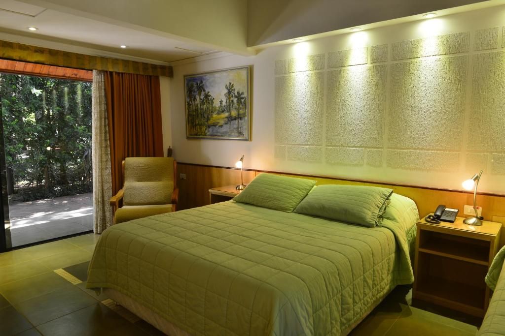 Quarto de hotel com uma cama grande, uma cadeira, mesa de cabeceira com telefone e um quadro na parede.