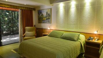 Quarto de hotel com uma cama grande, uma cadeira, mesa de cabeceira com telefone e um quadro na parede.