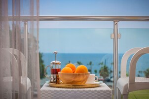 Uma varanda com uma mesa onde se encontram uma tigela de madeira com laranjas, uma xícara e uma cafeteira.