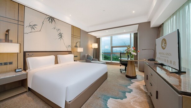 Quarto de hotel com uma cama grande, uma escrivaninha com computador, uma televisão e vista para a cidade.
