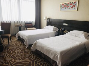 Quarto de hotel com duas camas, uma mesinha, uma cadeira, um abajur e um quadro na parede.