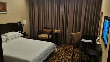 Quarto de hotel com cama, escrivaninha, cadeira, televisão e carpete estampado.