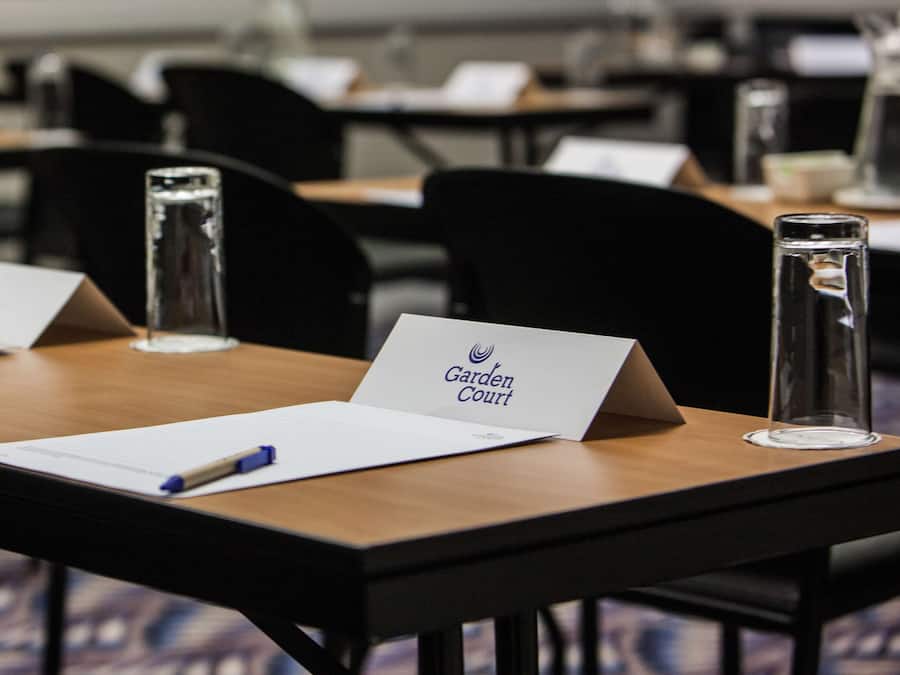 Uma sala de conferência com mesas equipadas com porta-nomes, canetas e garrafas de água de vidro.