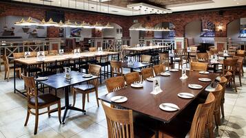 Um restaurante amplo com várias mesas e cadeiras, paredes de tijolo e luminárias modernas.