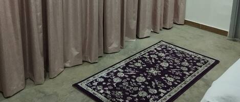 Quarto com cortinas bege, tapete estampado e uma cama.