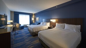 Quarto de hotel com duas camas, uma mesa com computador, uma cadeira e uma televisão.