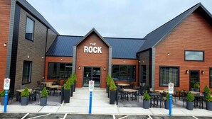 Um edifício com uma placa que diz "The Rock" e área externa com mesas e plantas em vasos.