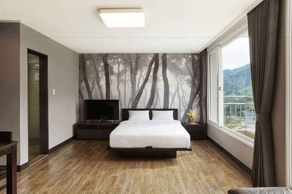 Quarto de hotel moderno com uma cama grande, uma TV de tela plana, mesa de cabeceira e vista para as montanhas pela janela.