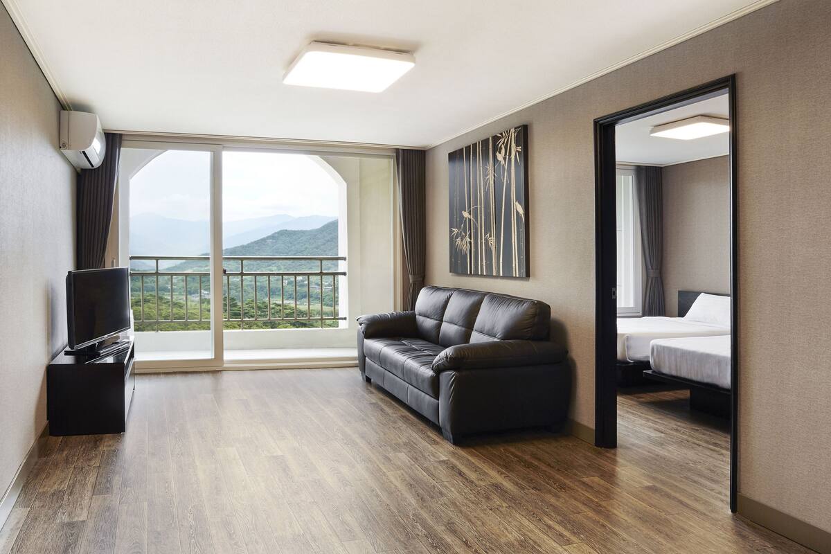 Quarto de hotel moderno com sofá de couro, televisão de tela plana, cama e uma grande janela com vista panorâmica.