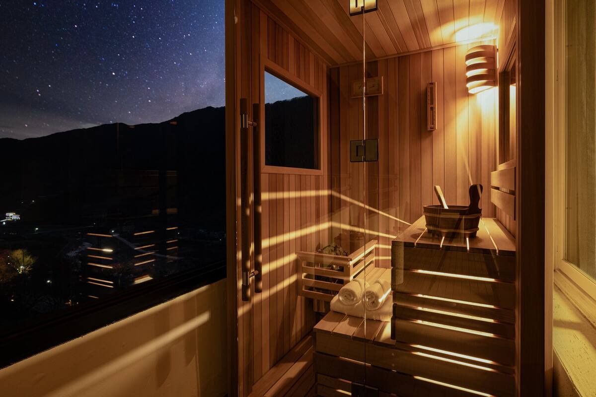 Uma sala de sauna de madeira com vista para uma noite estrelada pela janela, um banco de madeira e uma bacia de pedra.