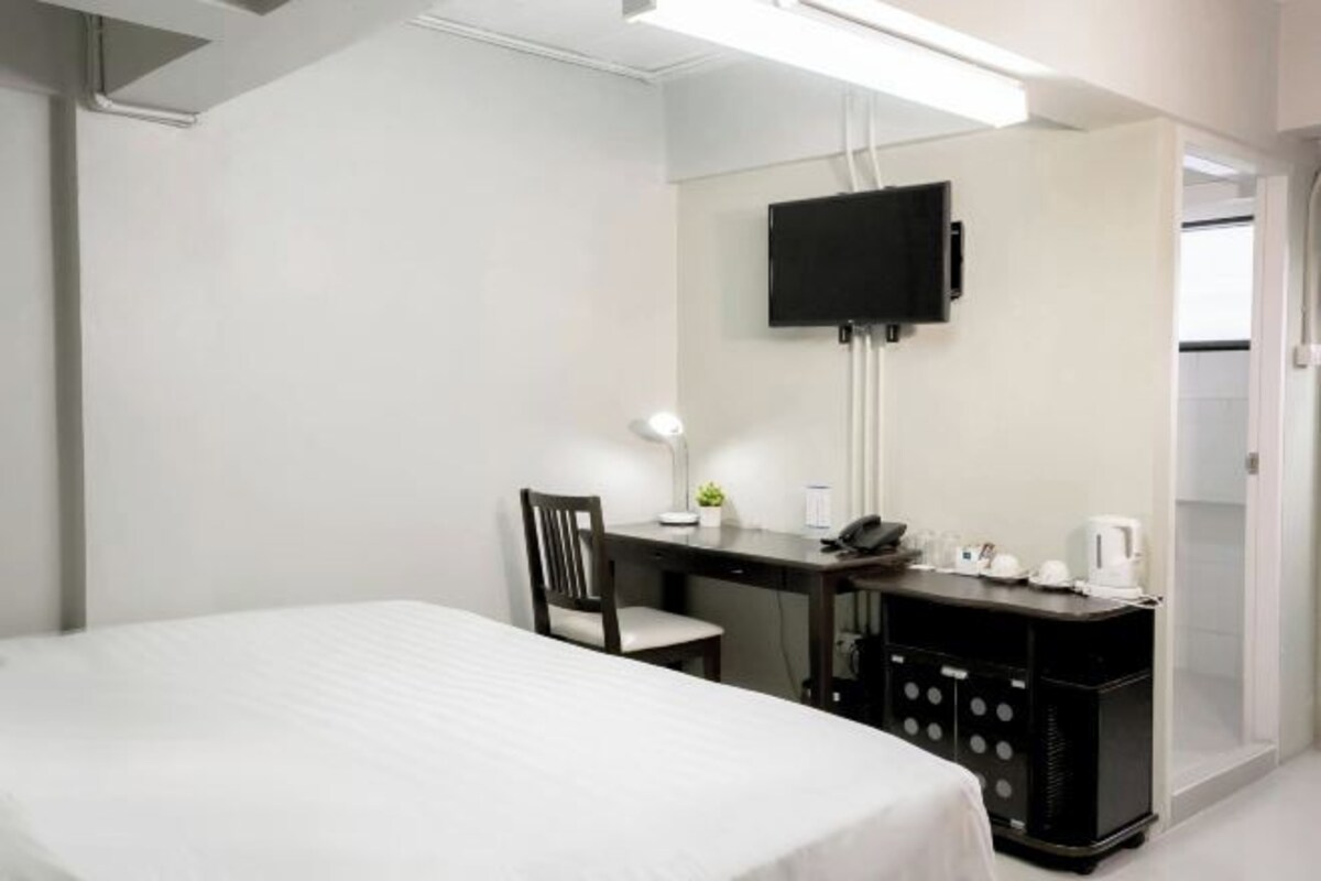 Quarto de hotel com cama, escrivaninha, cadeira, televisão presa na parede e minibar.