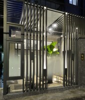 Uma entrada protegida por grade de metal, porta de vidro e um vaso de planta no interior.