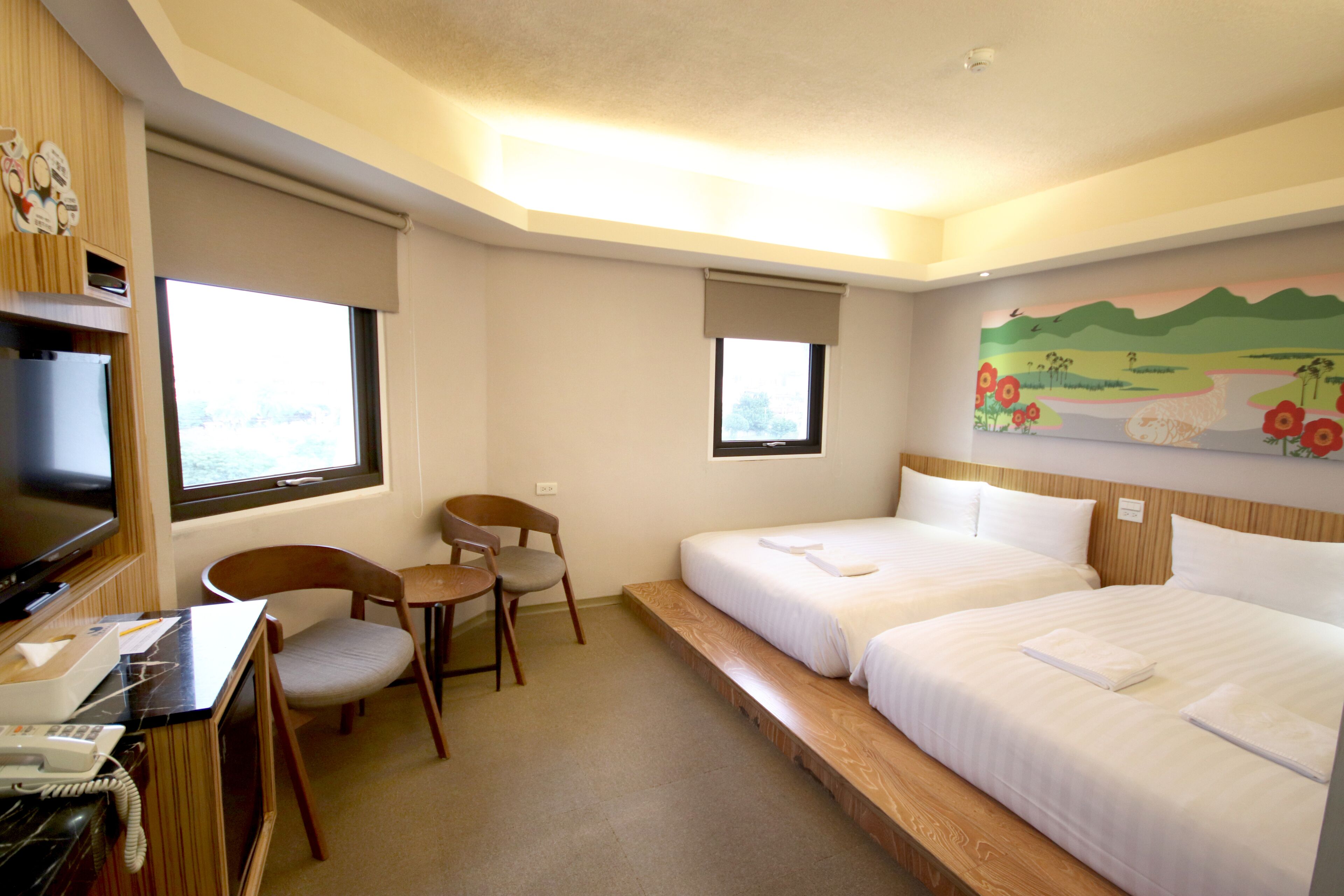 Quarto de hotel com duas camas, uma escrivaninha com cadeira, televisão e um quadro na parede.