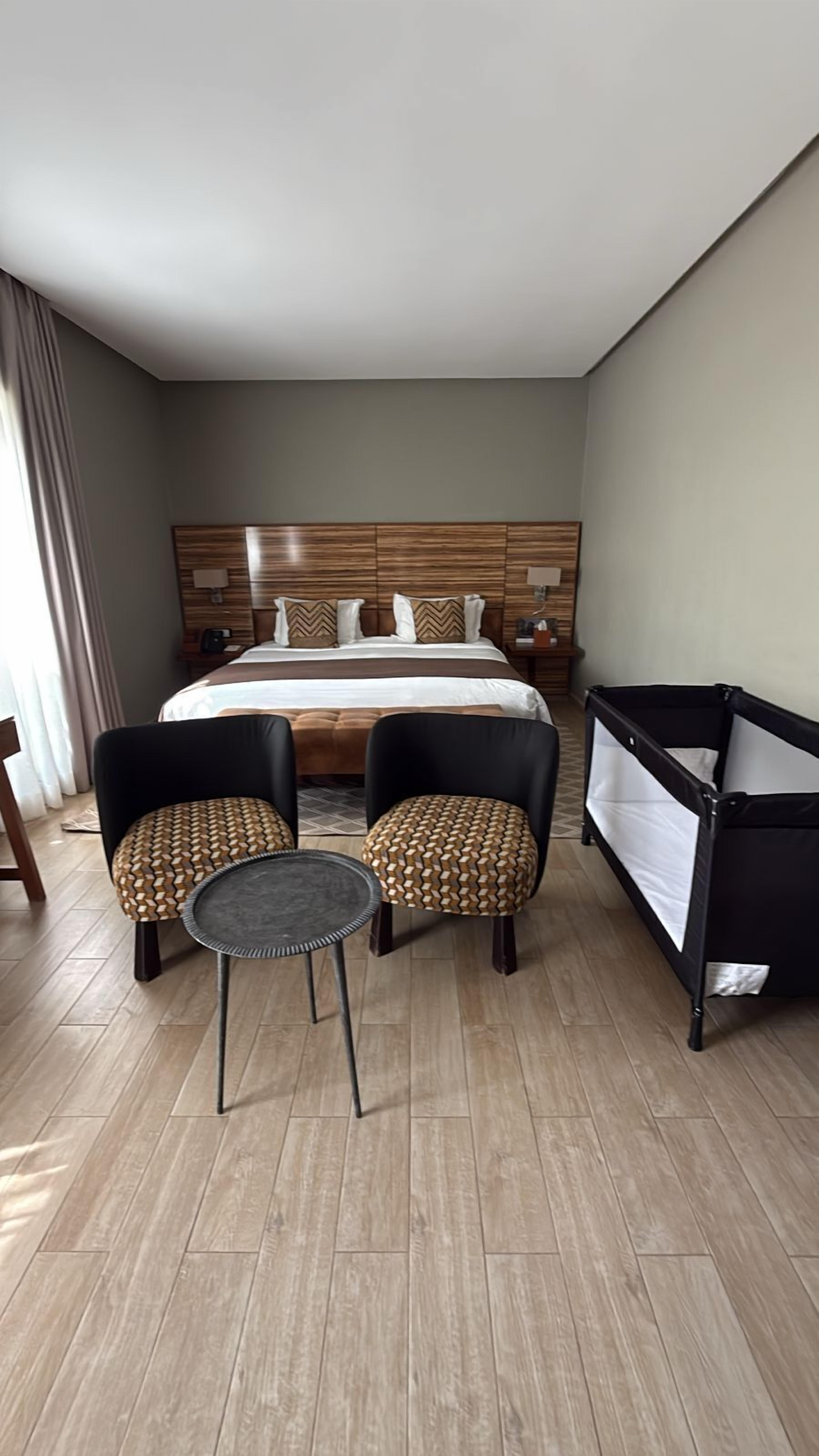 Quarto de hotel com cama, duas poltronas, uma mesinha e um berço.