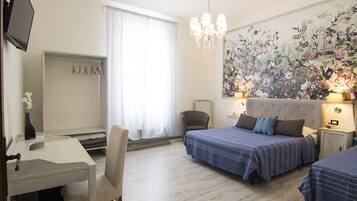 Quarto com duas camas, uma escrivaninha, uma cadeira, uma TV e um mural floral na parede.