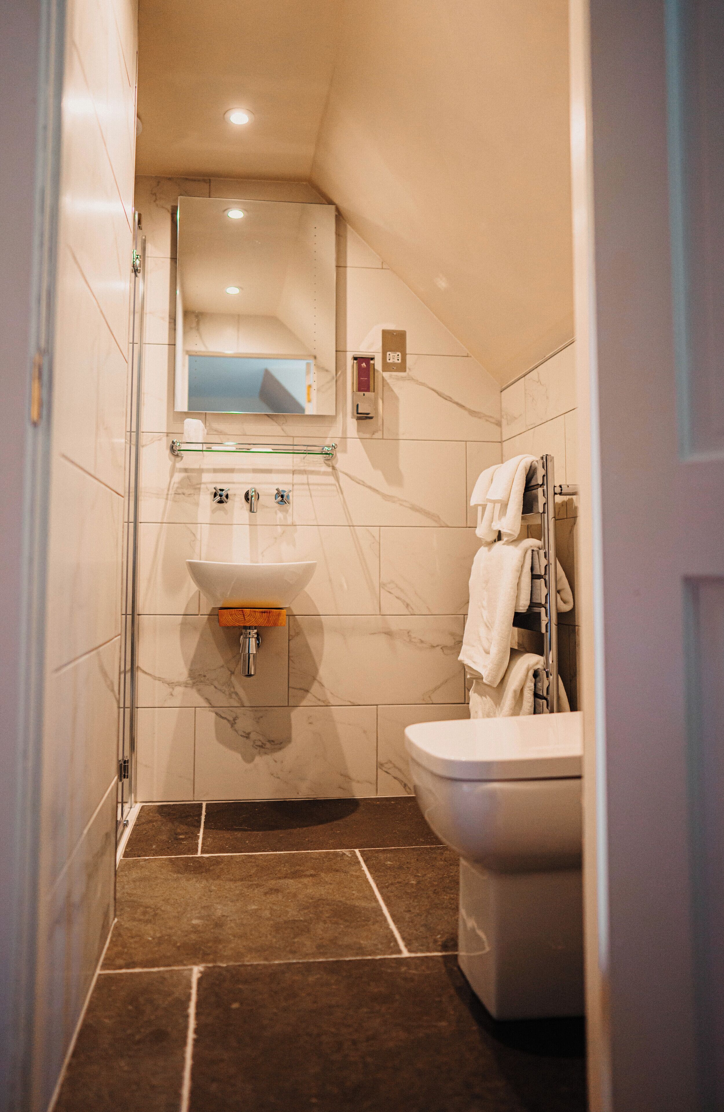Uma casa de banho pequena e moderna, com uma sanita, uma pia branca e cabine de duche em vidro.