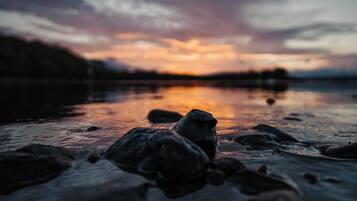 Um lago tranquilo ao pôr do sol, com rochas em primeiro plano.