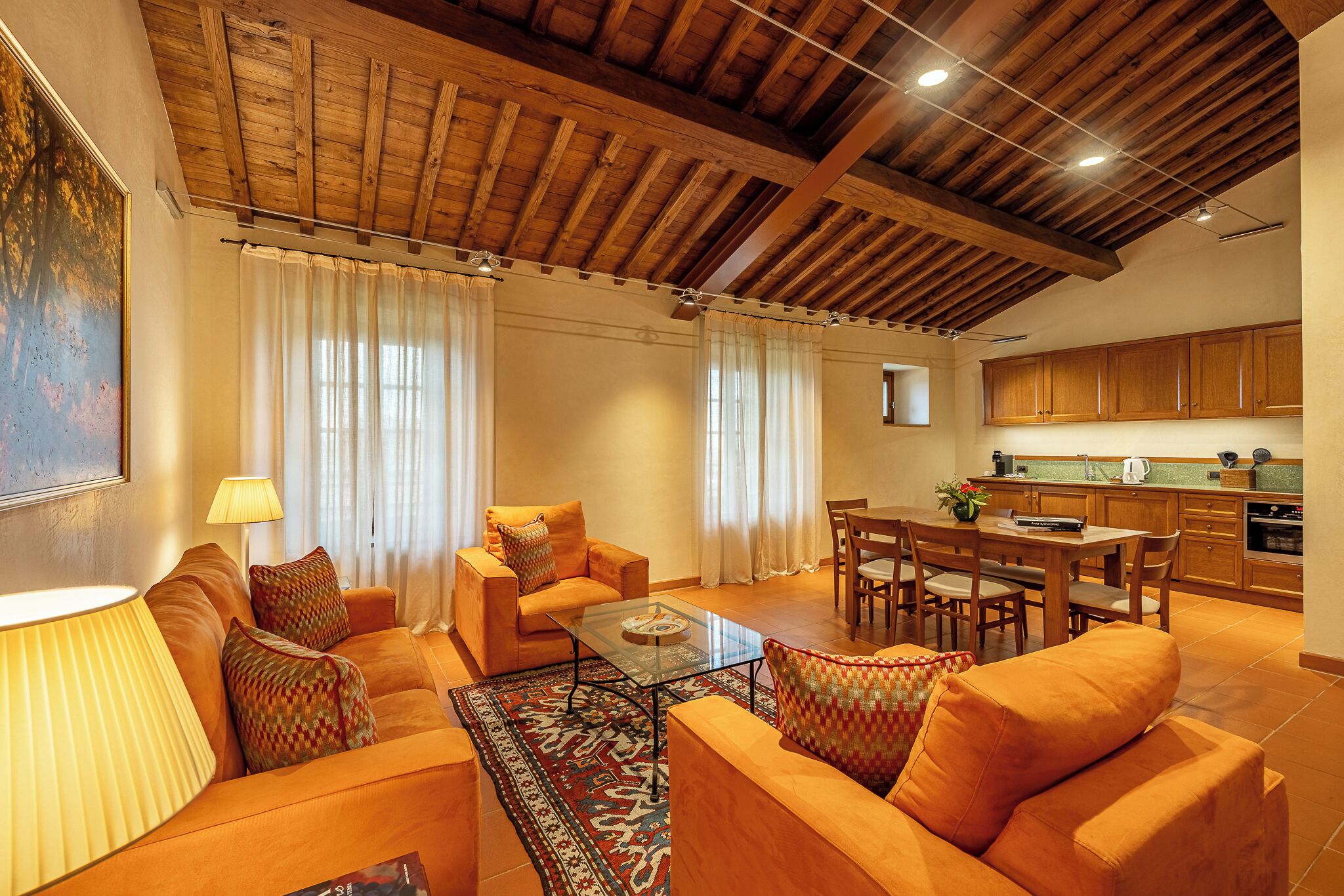 Uma sala de estar ampla com teto de madeira alto, mesa de jantar com cadeiras e cozinha com armários de madeira.