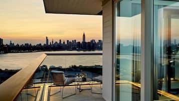 Uma varanda com mesa e cadeiras, com vista para o horizonte urbano e um corpo de água.