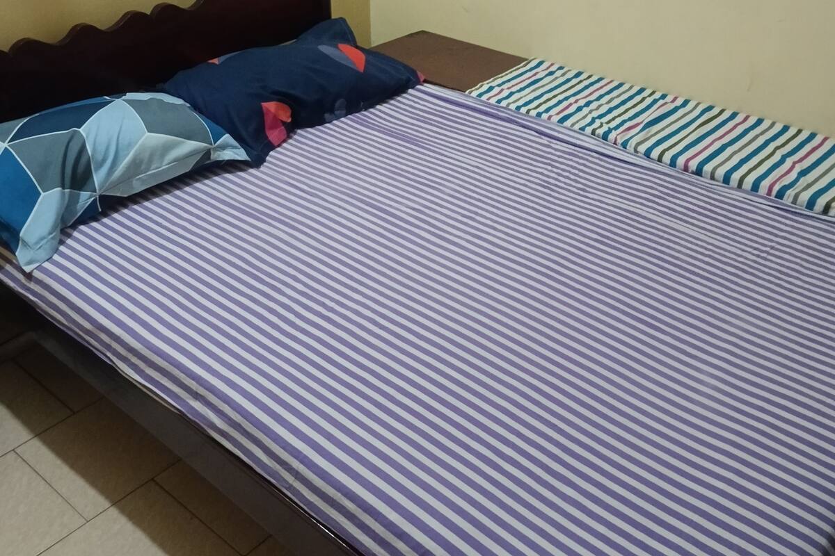 Uma cama com roupa de cama listrada e almofadas, uma cabeceira de madeira e uma parede lisa.