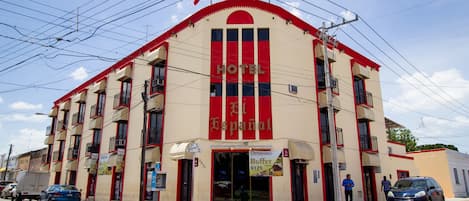 Um hotel com fachada em vermelho e bege, várias sacadas e uma placa indicando um buffet.