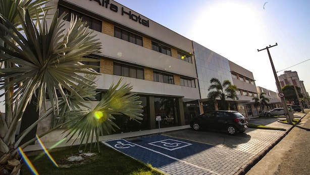 Hotel com fachada moderna, área de estacionamento com acessibilidade para pessoas com deficiência e céu claro.