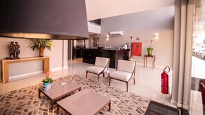 Um lobby de hotel moderno com área de estar, balcão de recepção e cozinha ao fundo.