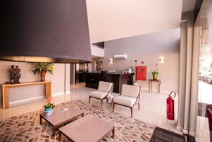 Um lobby de hotel moderno com área de estar, balcão de recepção e cozinha ao fundo.