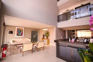 Um saguão de hotel com balcão de recepção, área de estar e uma grande obra de arte na parede.