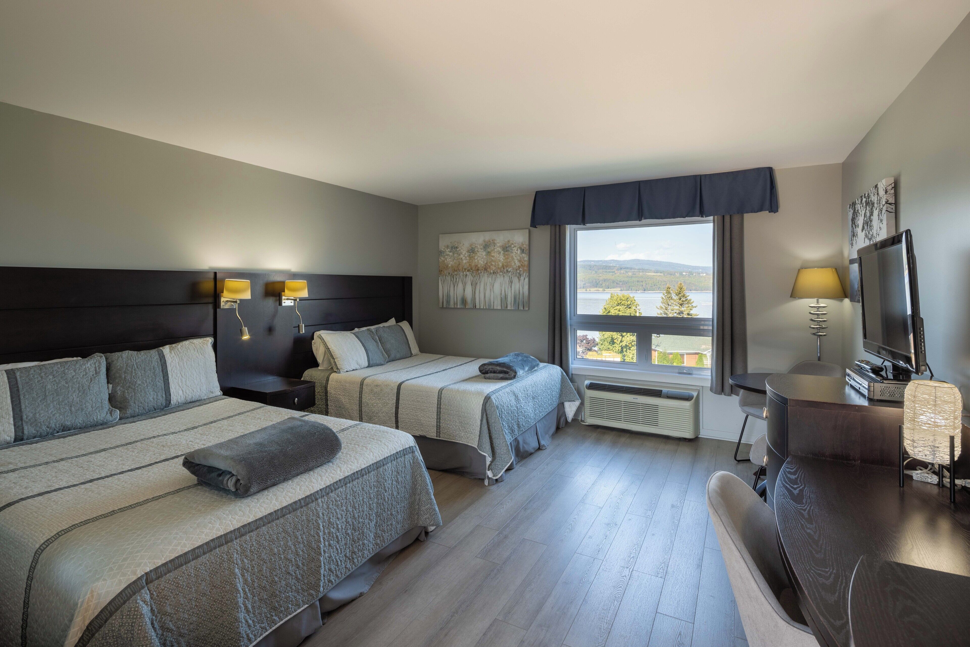 Quarto de hotel com duas camas, uma escrivaninha, televisão e janela com vista para o exterior.