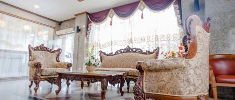 Um hall amplo com mobiliário requintado, um candelabro e uma janela grande com cortinas.