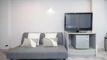 Uma sala de estar moderna com um sofá cinzento, duas almofadas brancas, uma TV de tela plana em um suporte e um refrigerador pequeno.