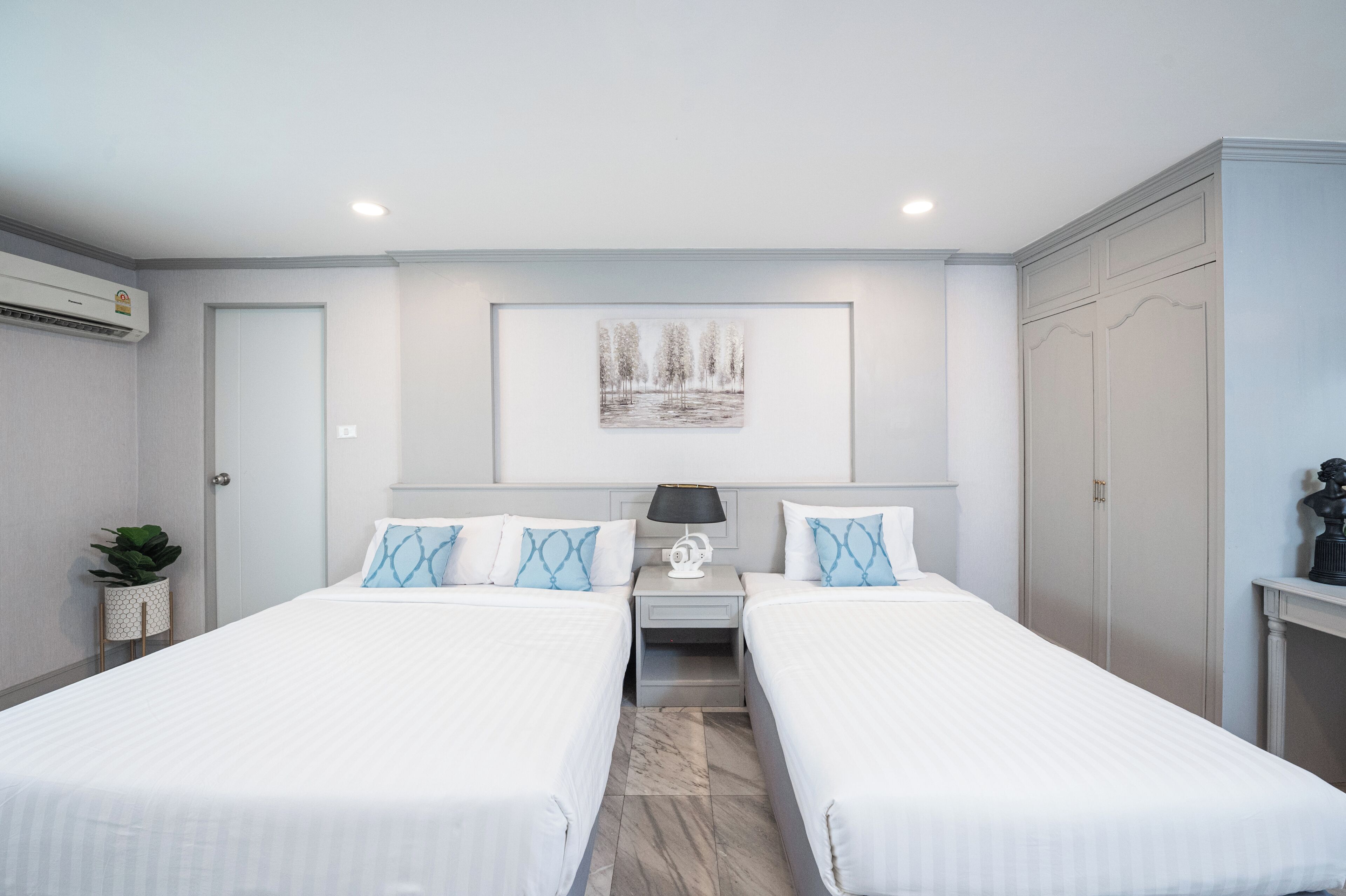 Quarto de hotel com duas camas, uma mesinha de cabeceira com abajur, um quadro pendurado na parede e um guarda-roupa.