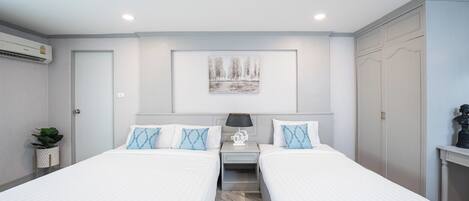 Quarto de hotel com duas camas, uma mesinha de cabeceira com abajur, um quadro pendurado na parede e um guarda-roupa.