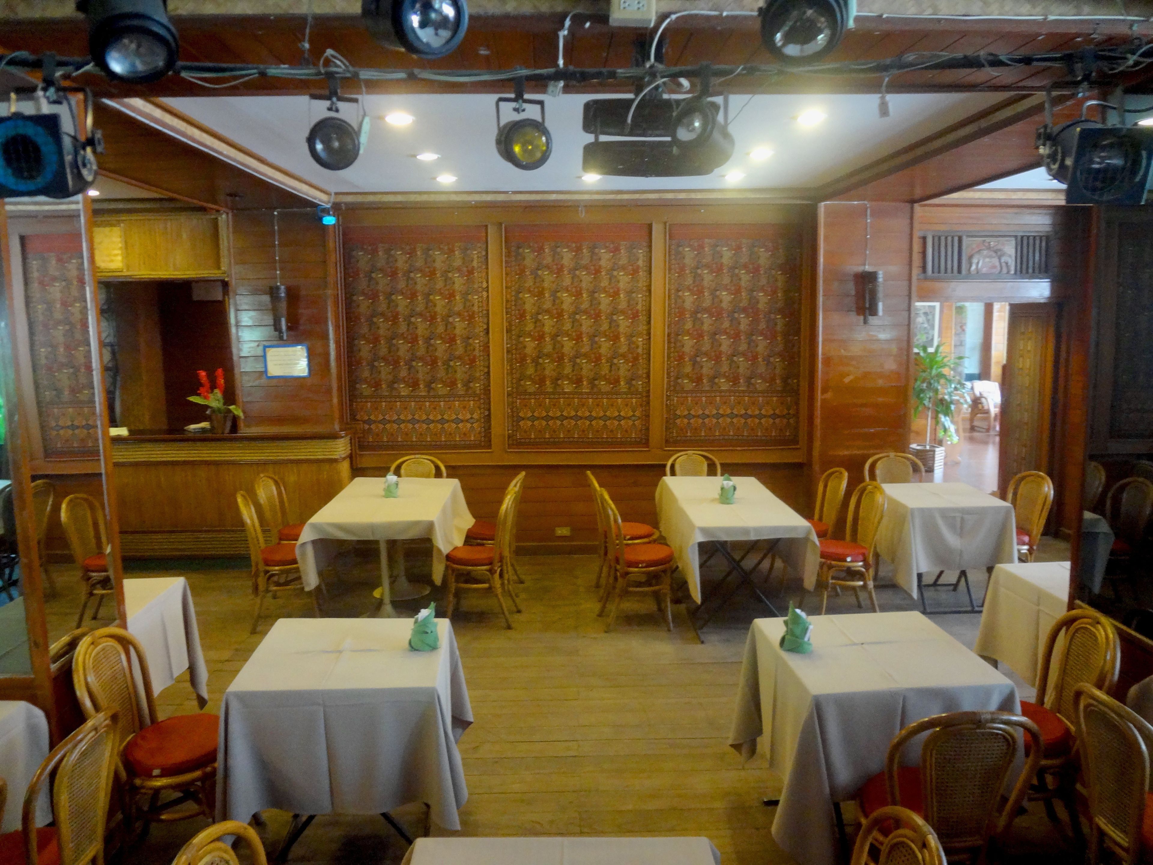 Um restaurante com várias mesas e cadeiras, painéis de madeira nas paredes e luminárias no teto.