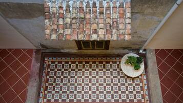 Piso de azulejos com padrão geométrico, um pequeno cachepot com planta e teto de azulejos com moldura decorativa.