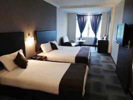 Quarto de hotel com duas camas, uma escrivaninha, uma cadeira e uma televisão.
