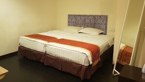Uma cama de casal com cabeceira estampada, base marrom com saia e colcha branca.